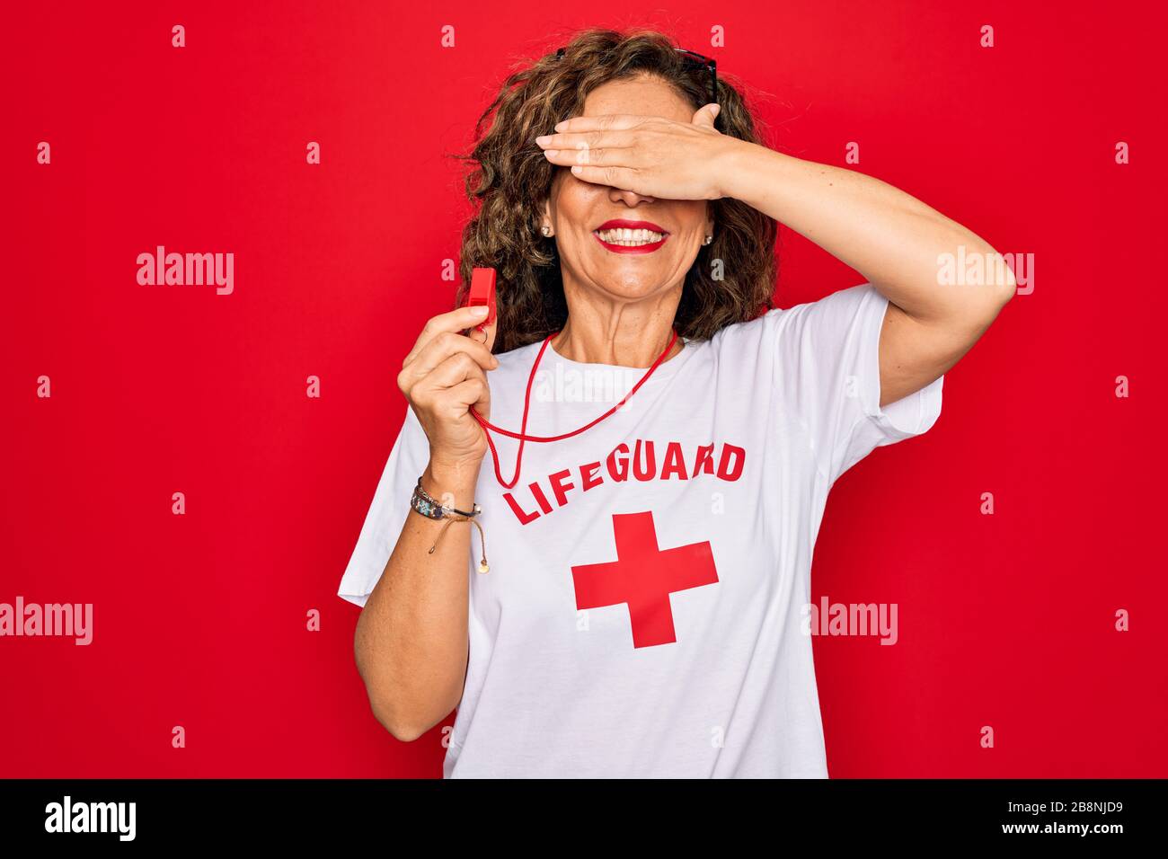 Middle age senior summer lifeguard woman holding whistle over red ...