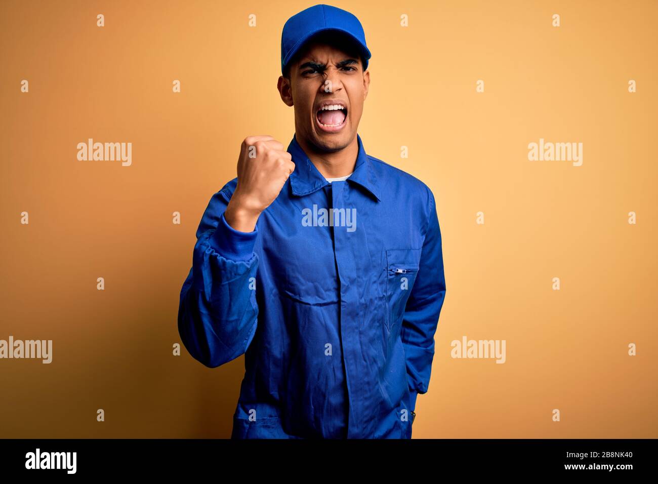 Young african american mechanic man wearing blue uniform and cap over ...