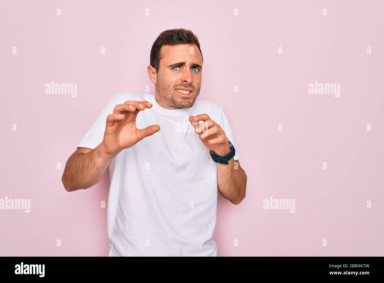 Handsome man with blue eyes wearing casual white t-shirt standing over ...