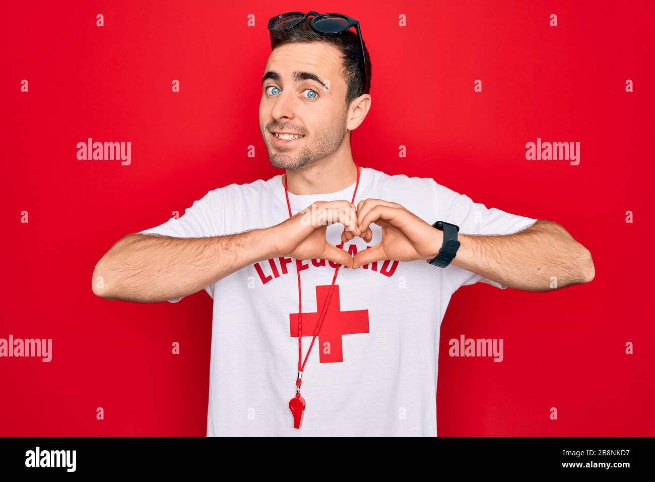 Handsome lifeguard man wearing t-shirt with red cross and whistle over ...