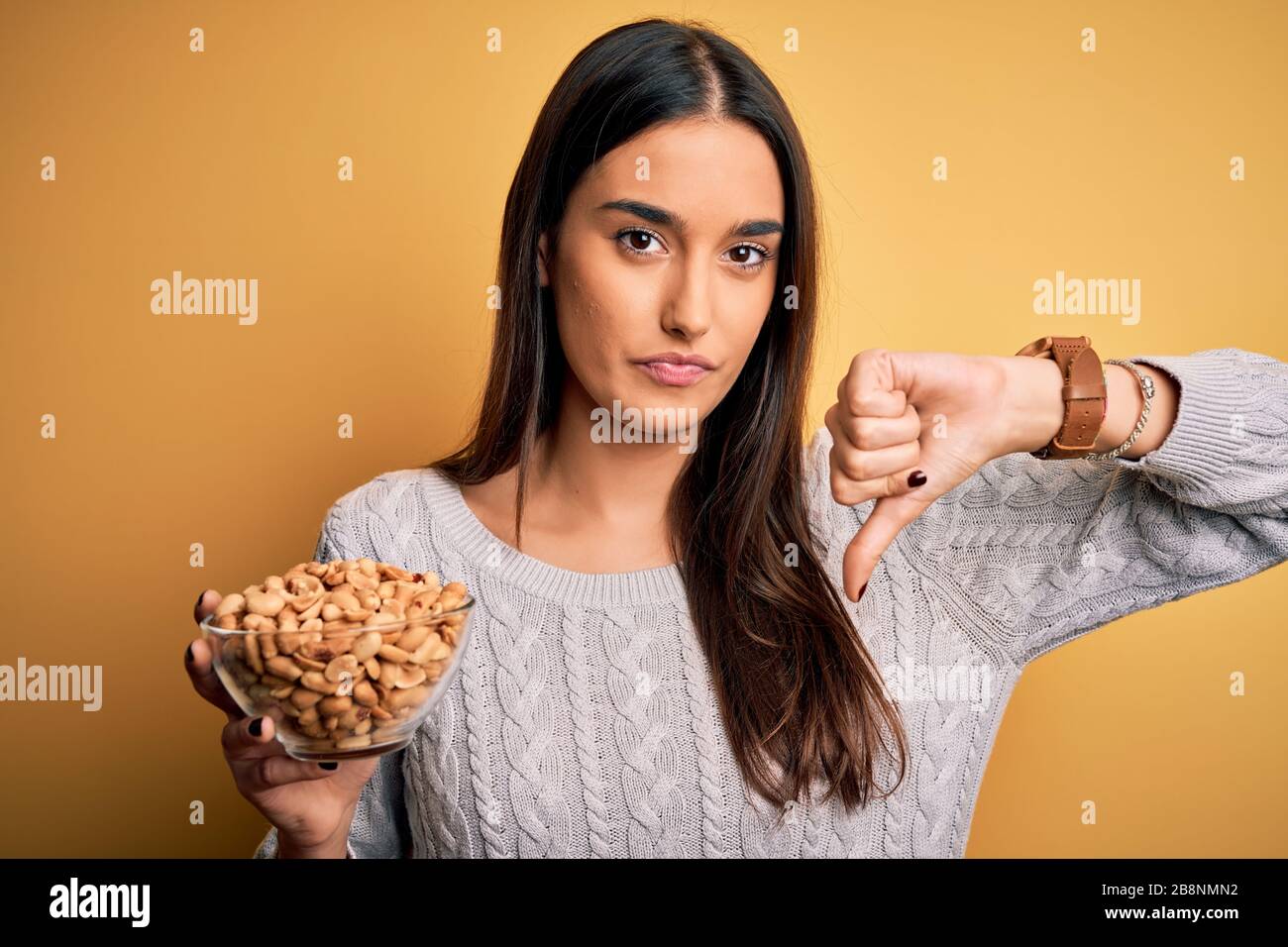 Young beautiful brunette woman holding bowl with peanuts over isolated ...