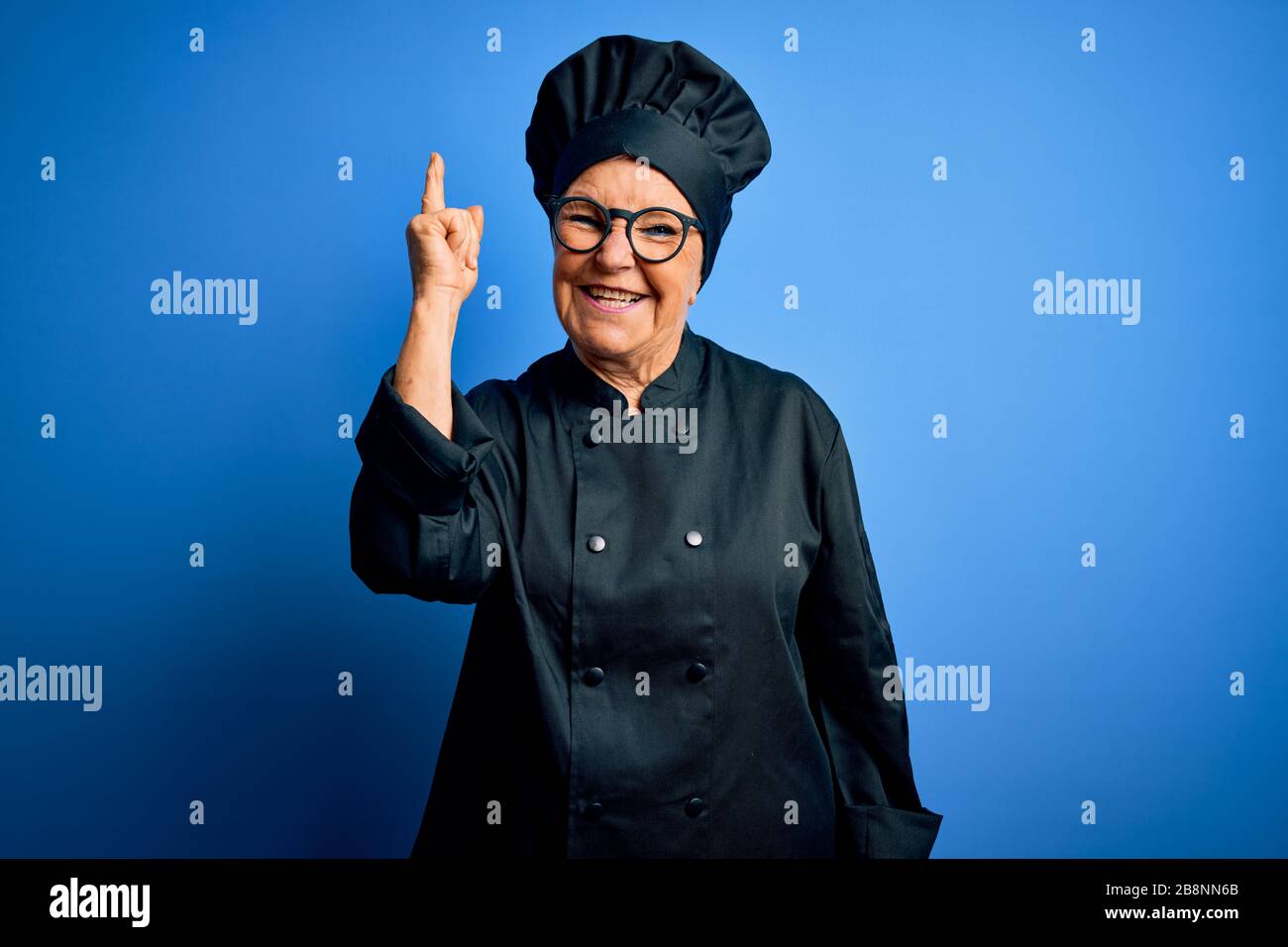 Senior beautiful grey-haired chef woman wearing cooker uniform and hat ...