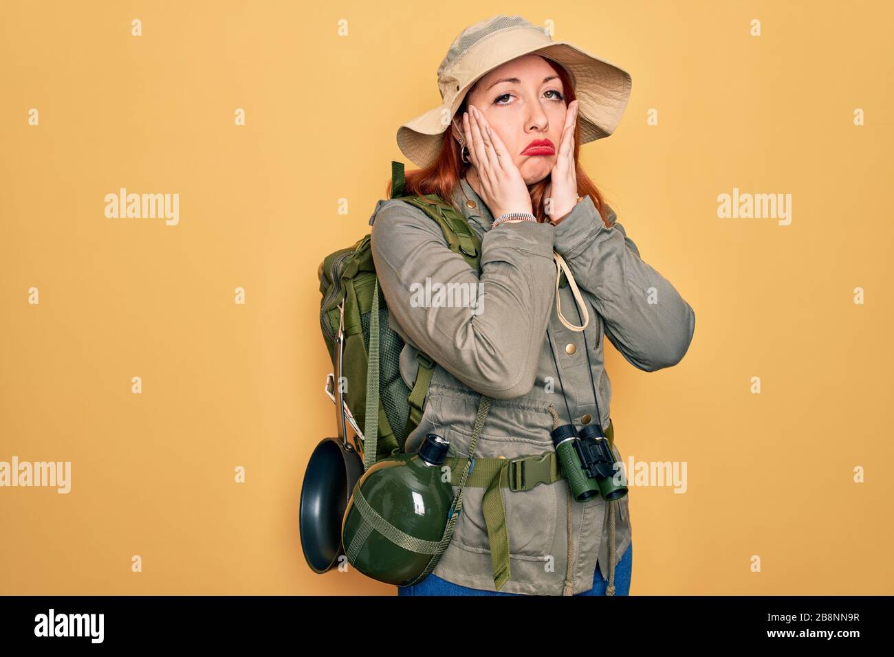 Young redhead backpacker woman hiking wearing backpack and hat over ...