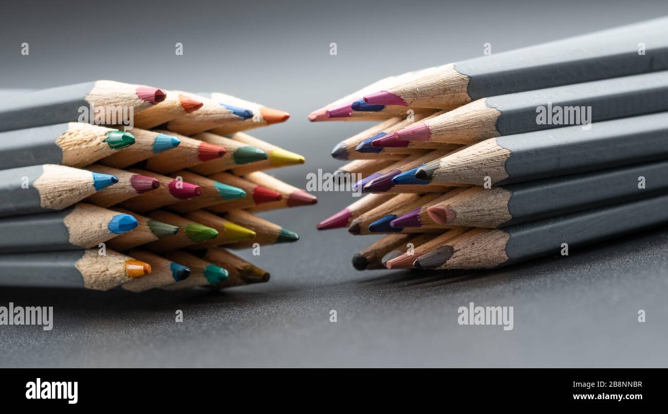 A closeup image of two opposing sets of coloured pencils on a grey ...