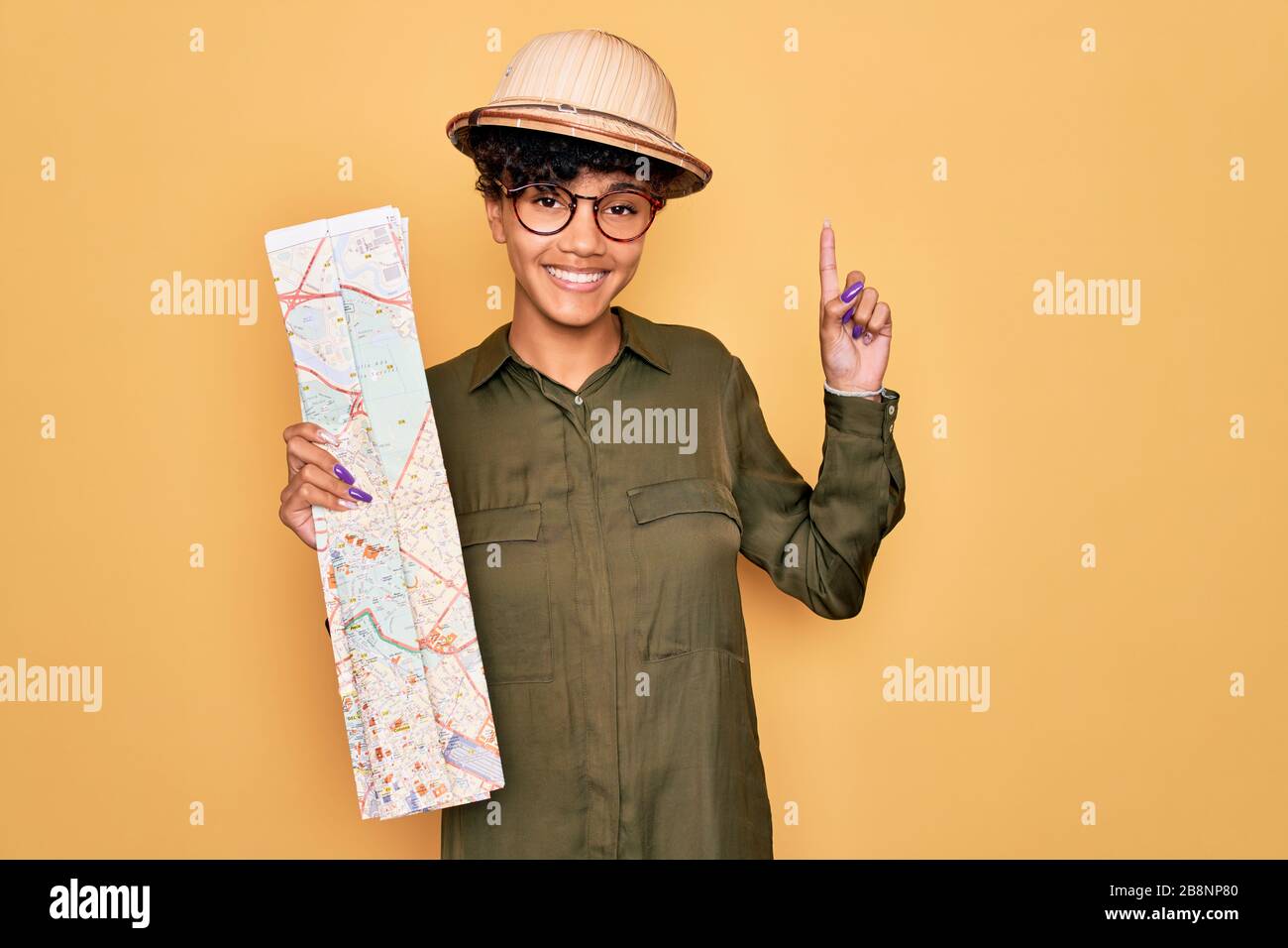 Beautiful african american explorer woman wearing hat holding city map ...
