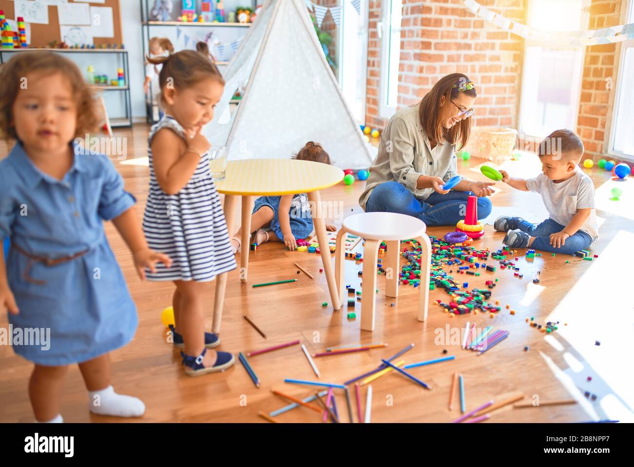 Beautiful teacher and group of toddlers playing around lots of toys at ...