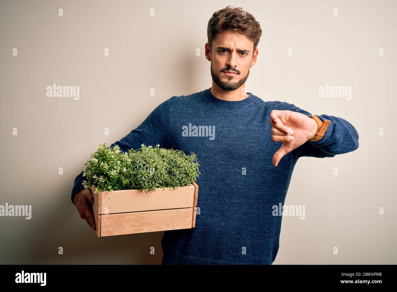 Young gardener man with beard holding box with plants standing over ...