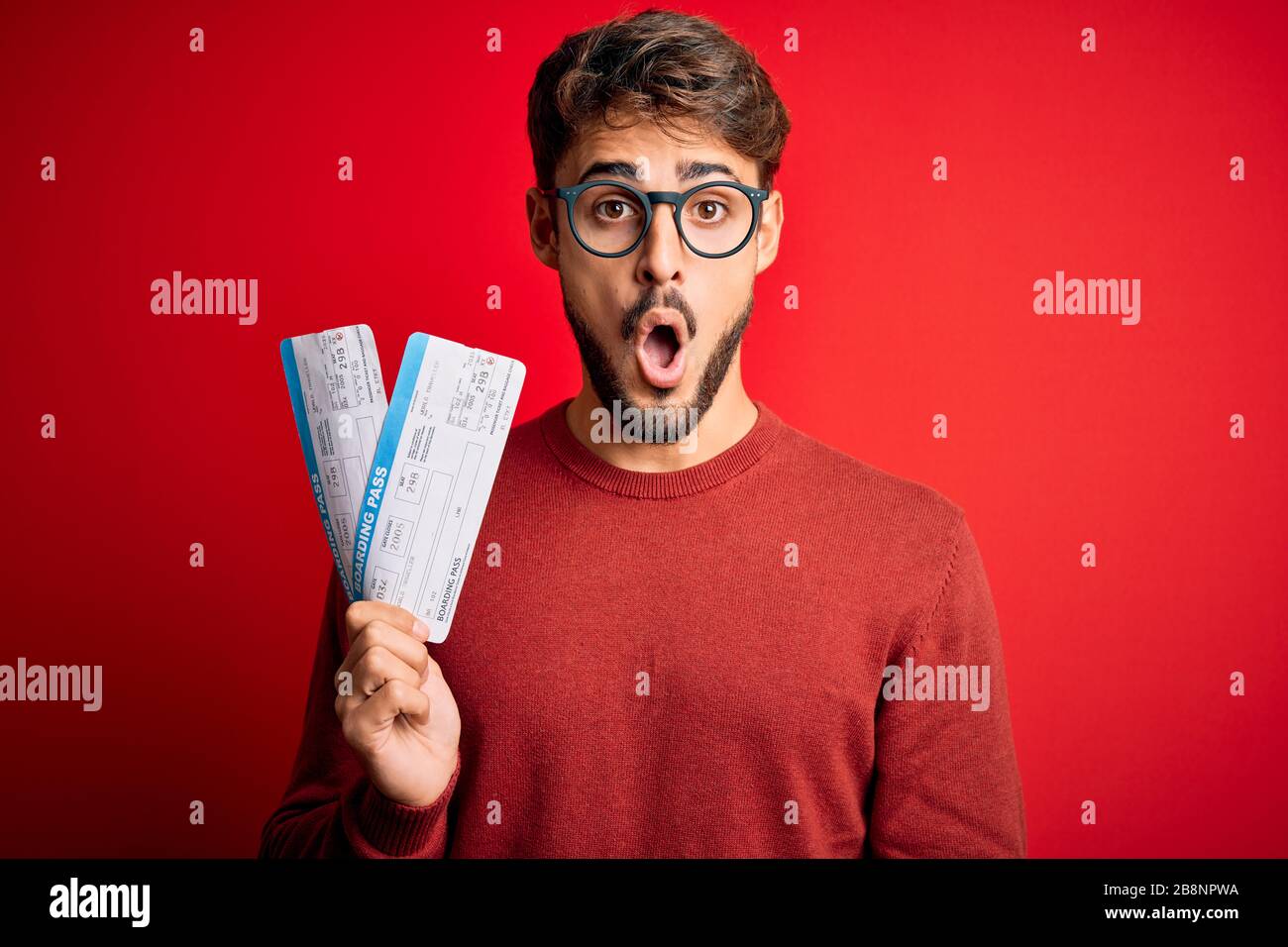 Young tourist man on vacation holding boarding pass standing over red ...