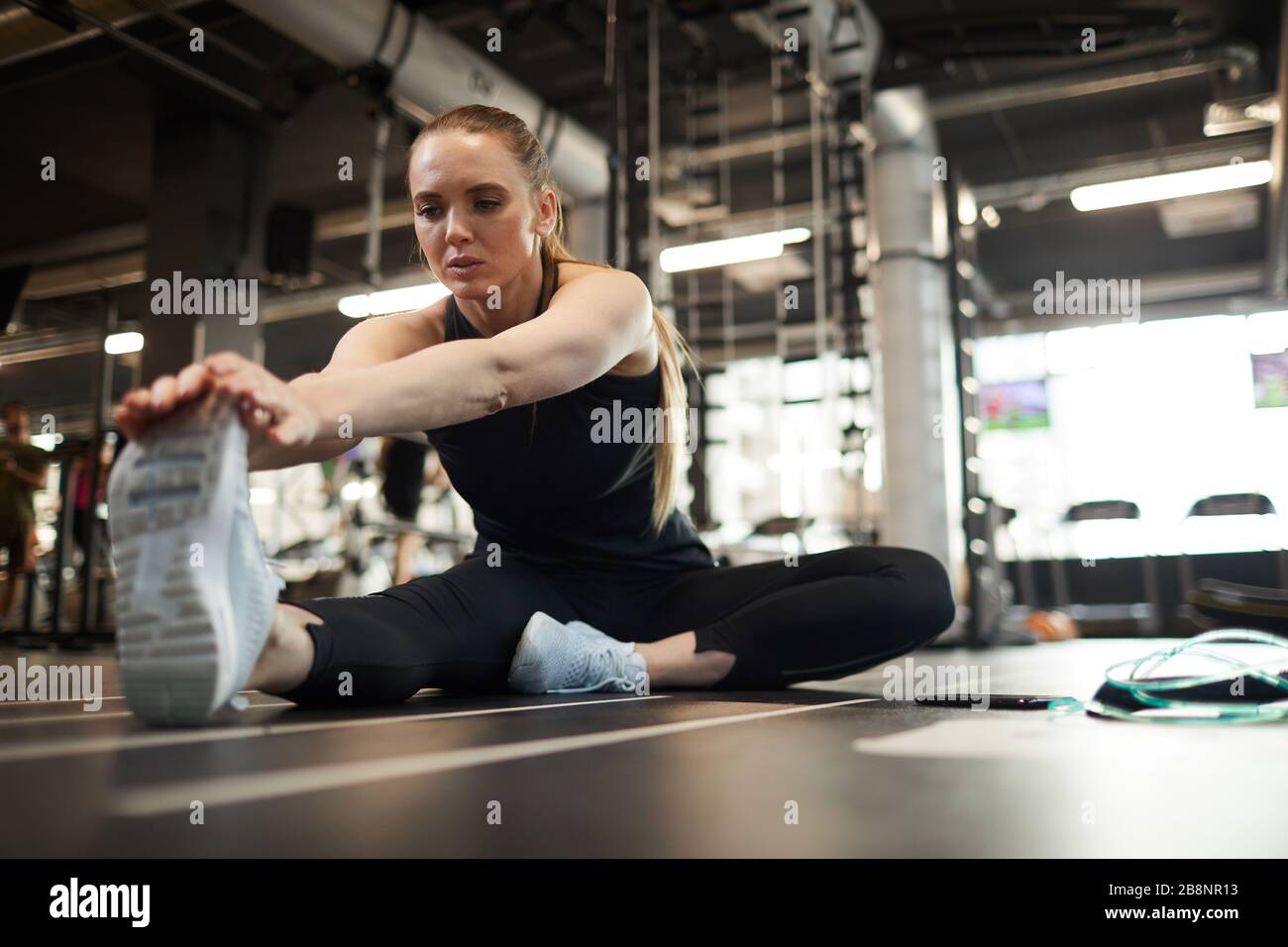 Full length portrait of blond young woman stretching legs while ...