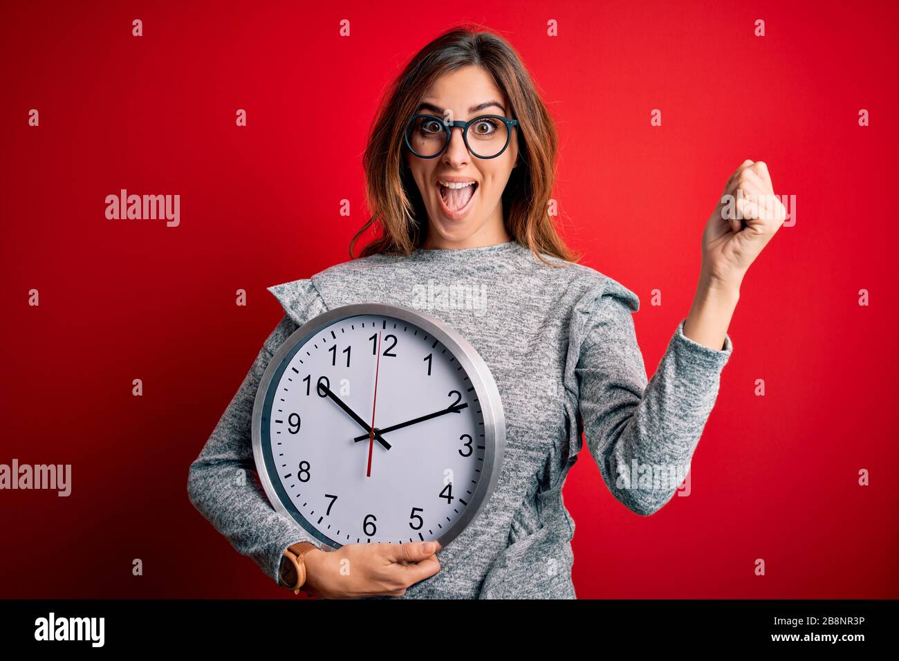 Young beautiful brunette woman doing countdown holding big clock over ...
