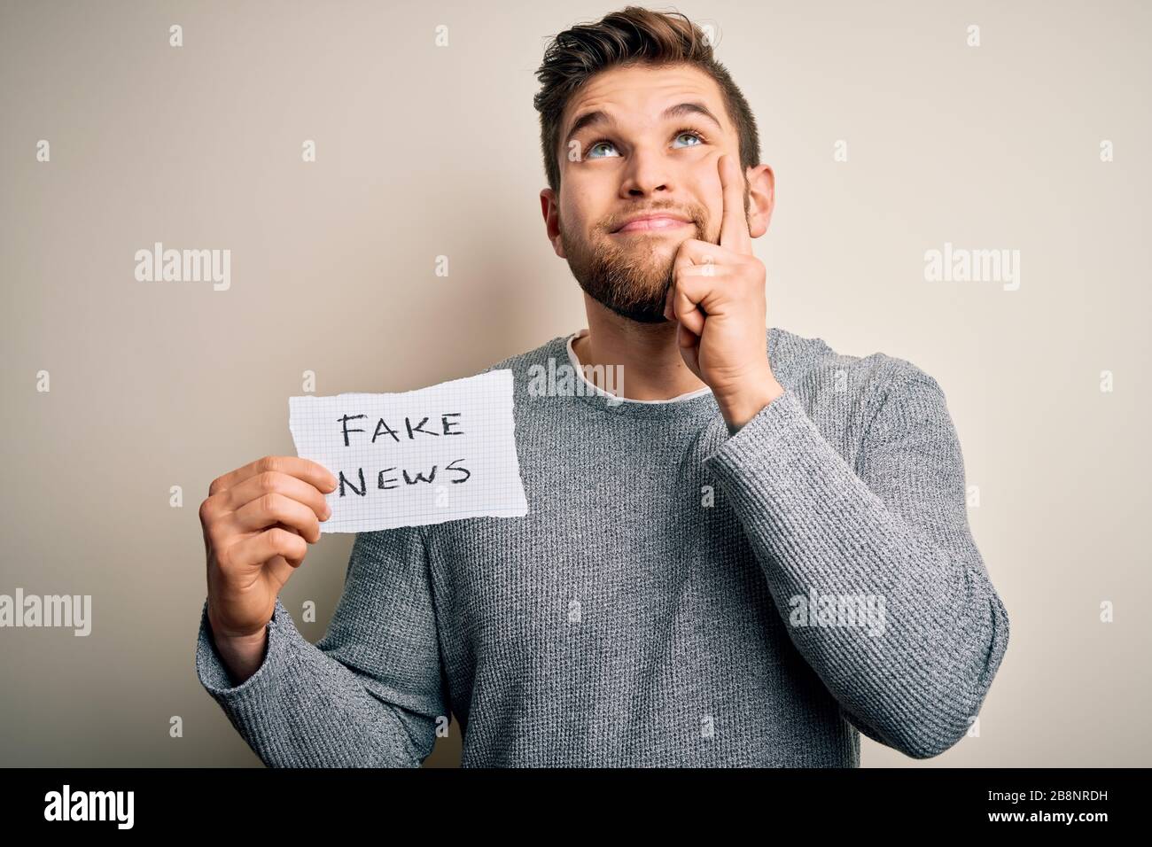 Young blond man with beard and blue eyes holding paper with fake news ...