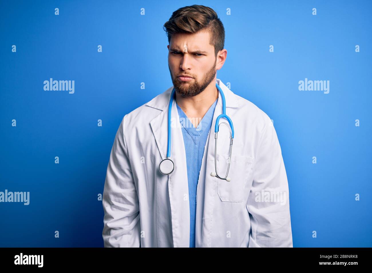 Young blond doctor man with beard and blue eyes wearing white coat and ...