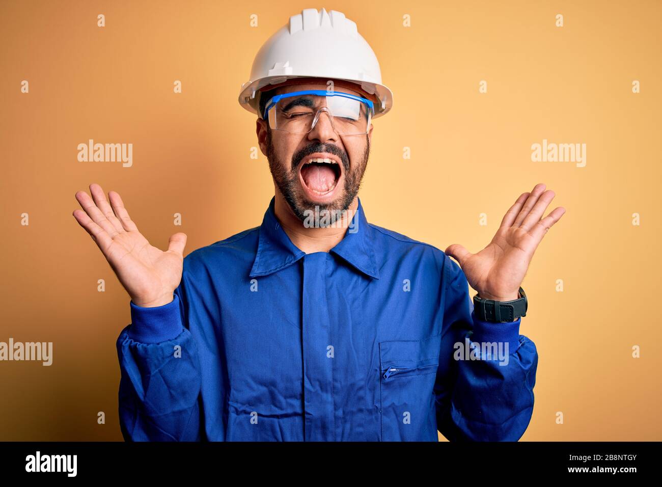 Mechanic man with beard wearing blue uniform and safety glasses over ...