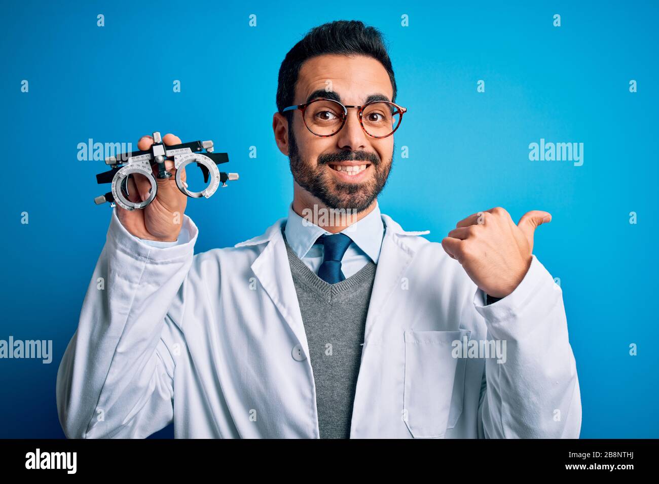 Young handsome optical man with beard holding optometry glasses over ...