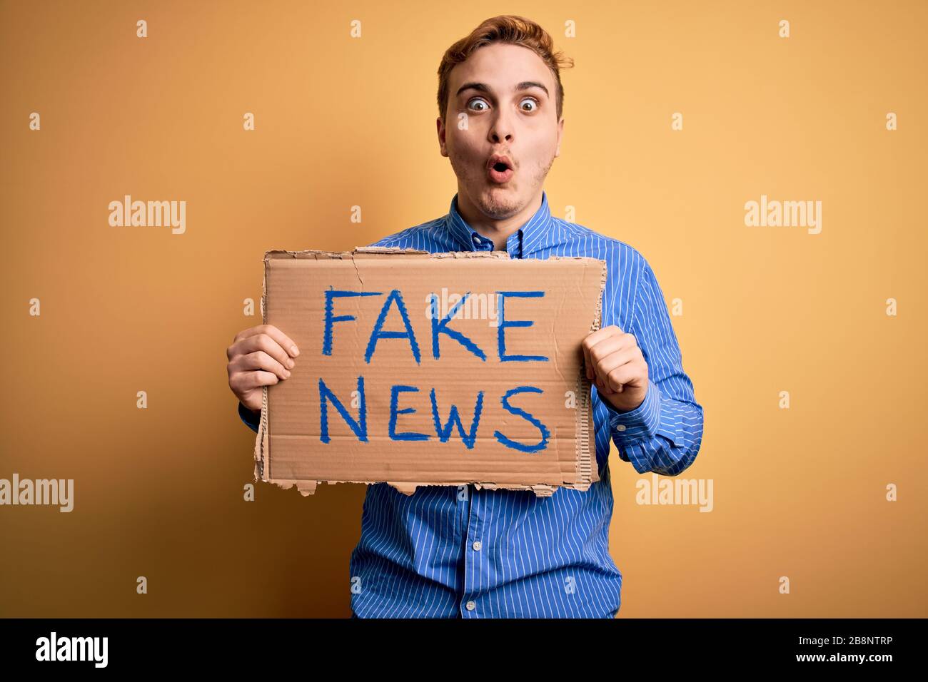 Young handsome redhead man holding banner with fake news message over ...