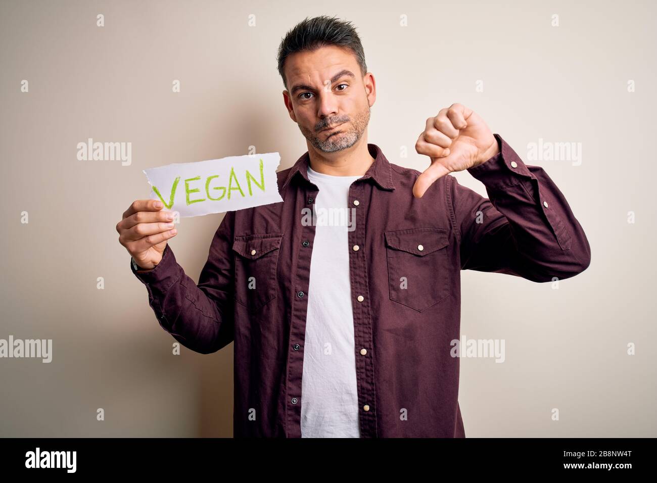 Young handsome veggie man holding paper with vegan message over white ...