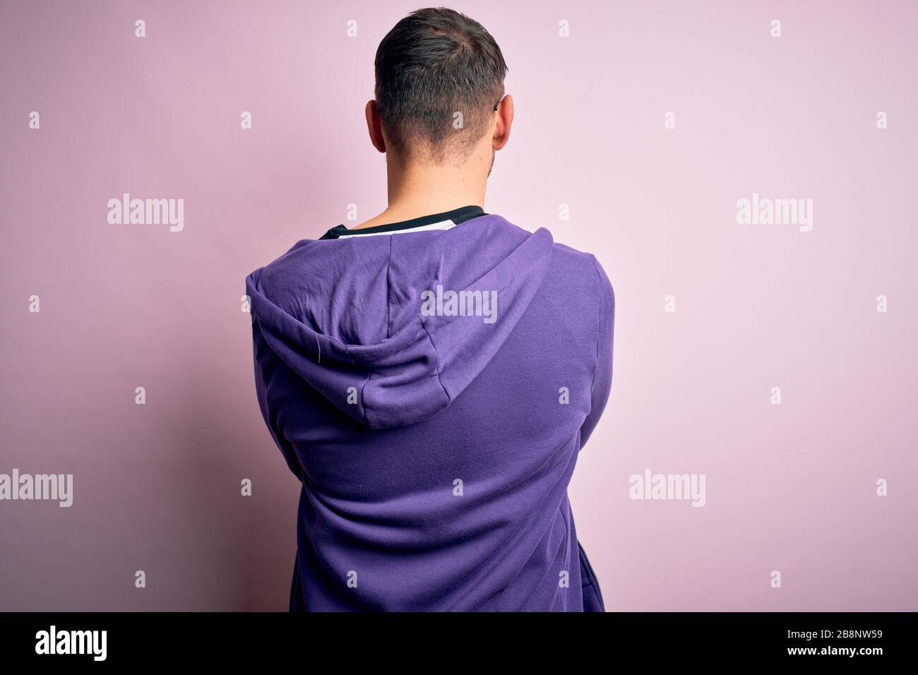 Young handsome man wearing purple sweatshirt and glasses standing over ...