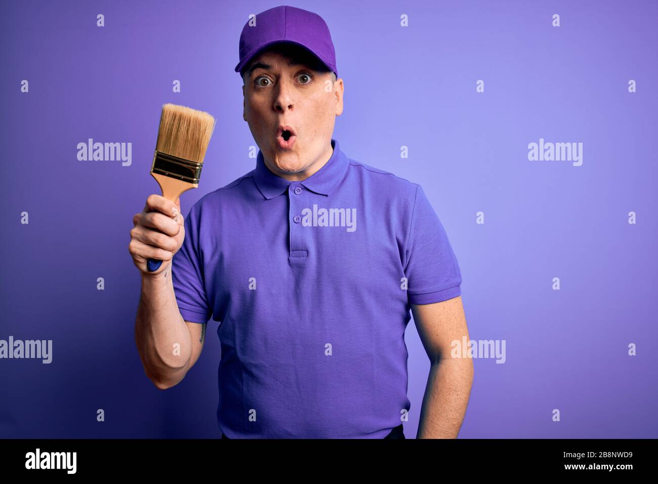 Young modern decorator painter man holding paint brush over purple ...