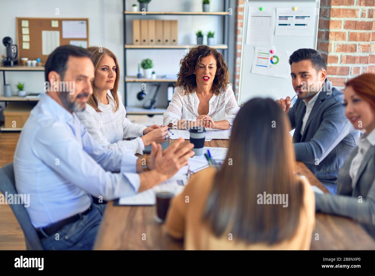 Group of business workers working together. Sitting on desk speaking at ...