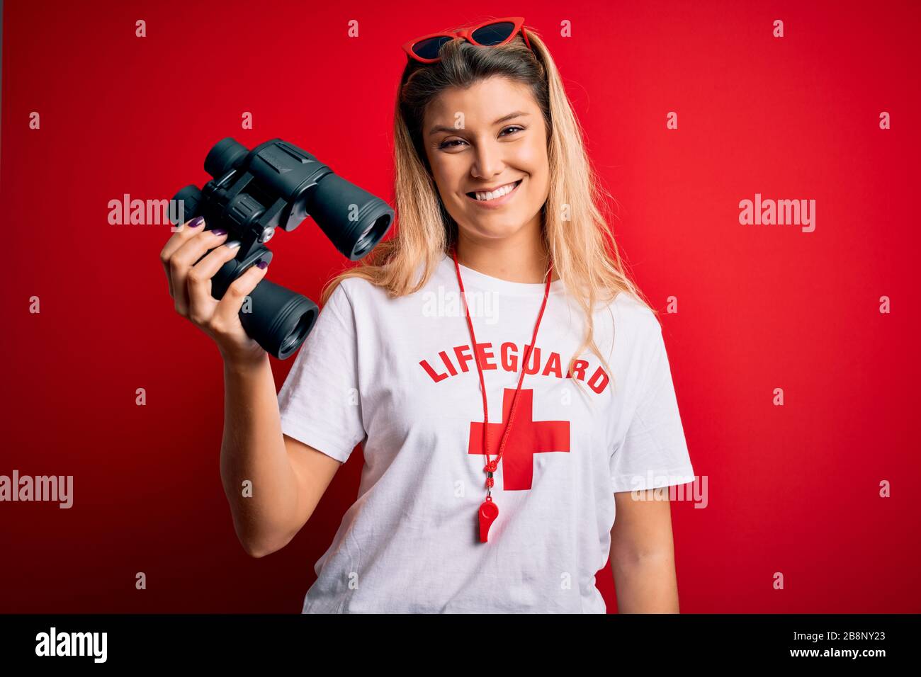 Young beautiful blonde lifeguard woman using binoculars and whistle ...