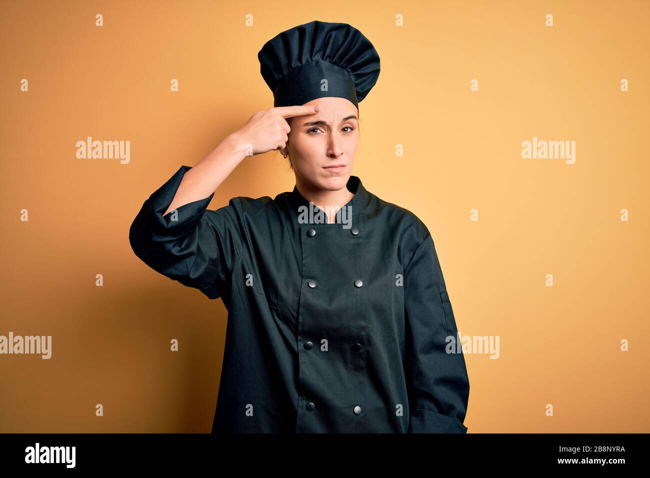 Young beautiful chef woman wearing cooker uniform and hat standing over ...