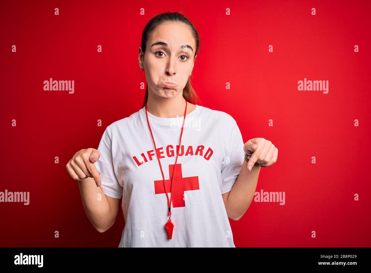 Beautiful lifeguard woman wearing t-shirt with red cross using whistle ...