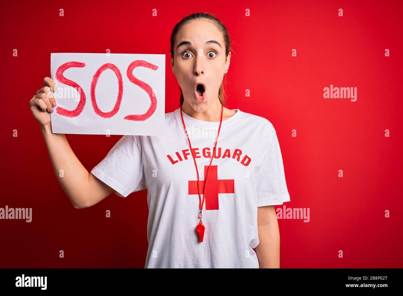 Lifeguard woman wearing t-shirt with red cross and whistle holding ...