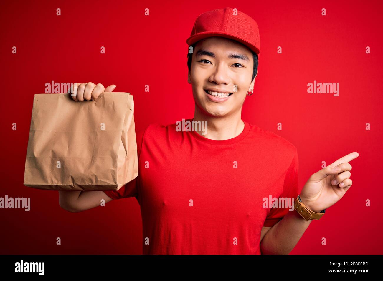 Young handsome chinese delivery man holding takeaway paper bag with ...