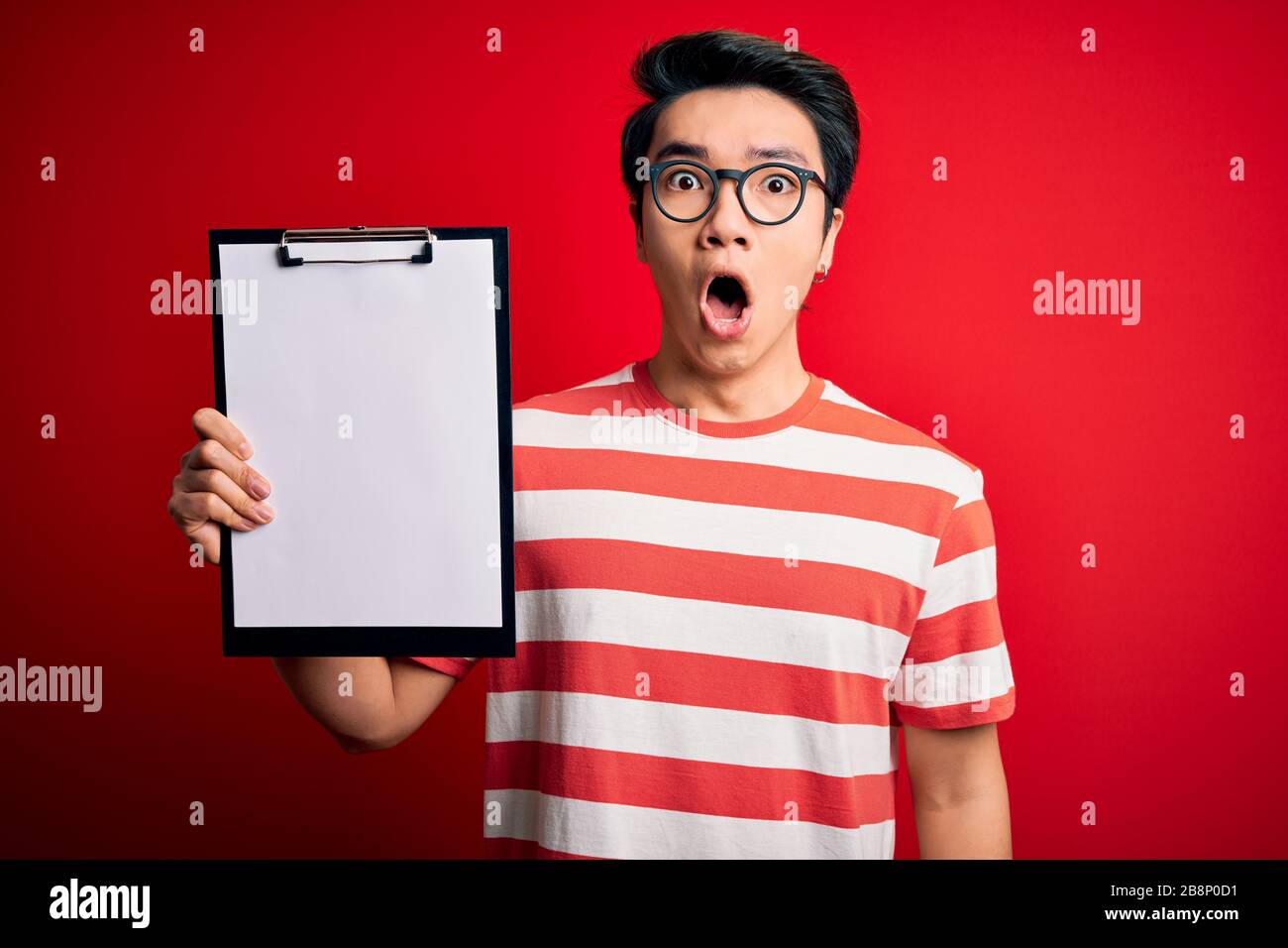Young handsome chinese inspector man wearing glasses holding clipboard ...