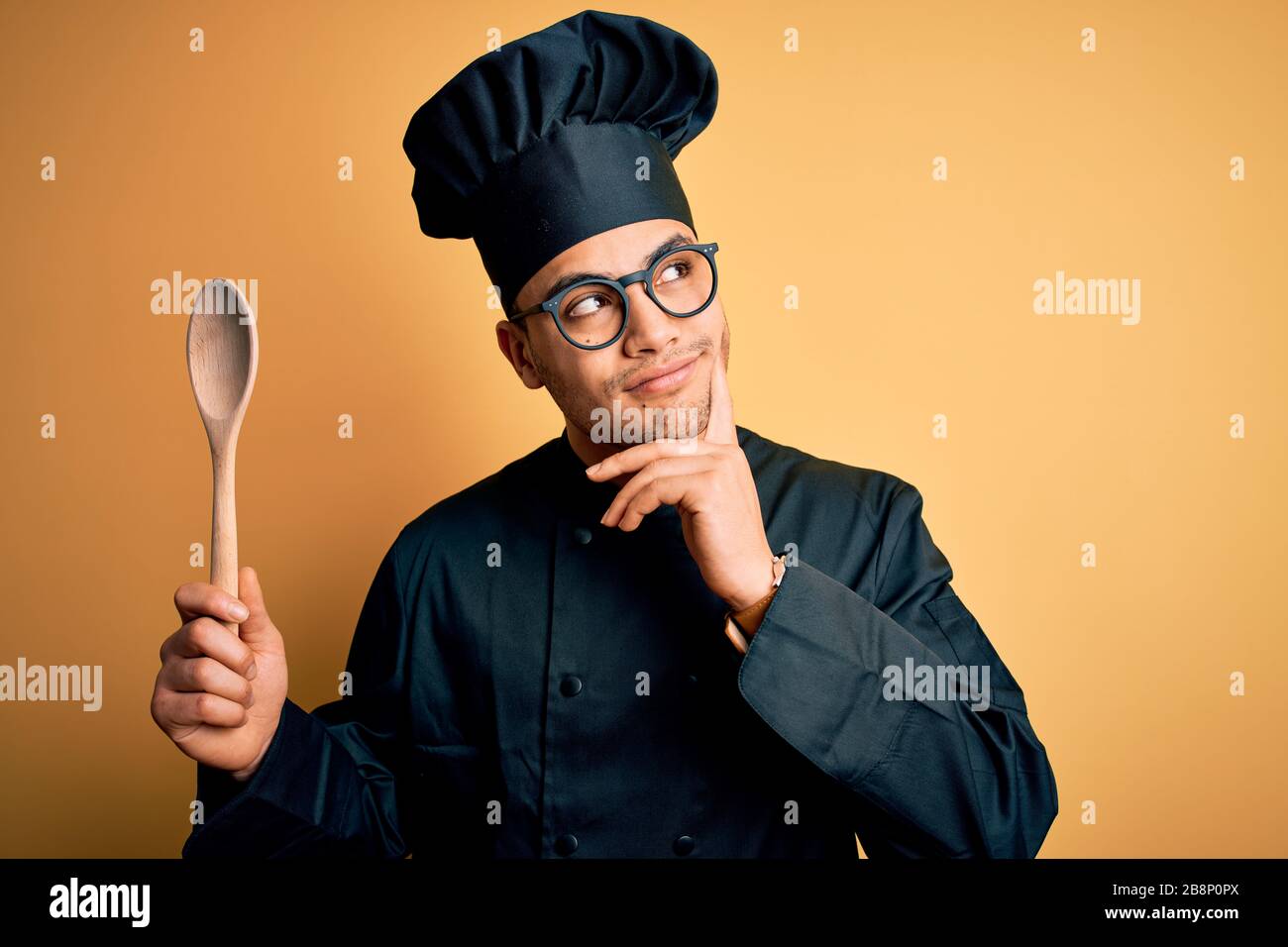 Young brazilian chef man wearing cooker uniform and hat holding wooden ...
