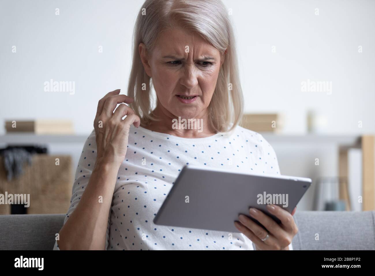 Frowning middle aged woman looking at computer tablet Stock Photo - Alamy