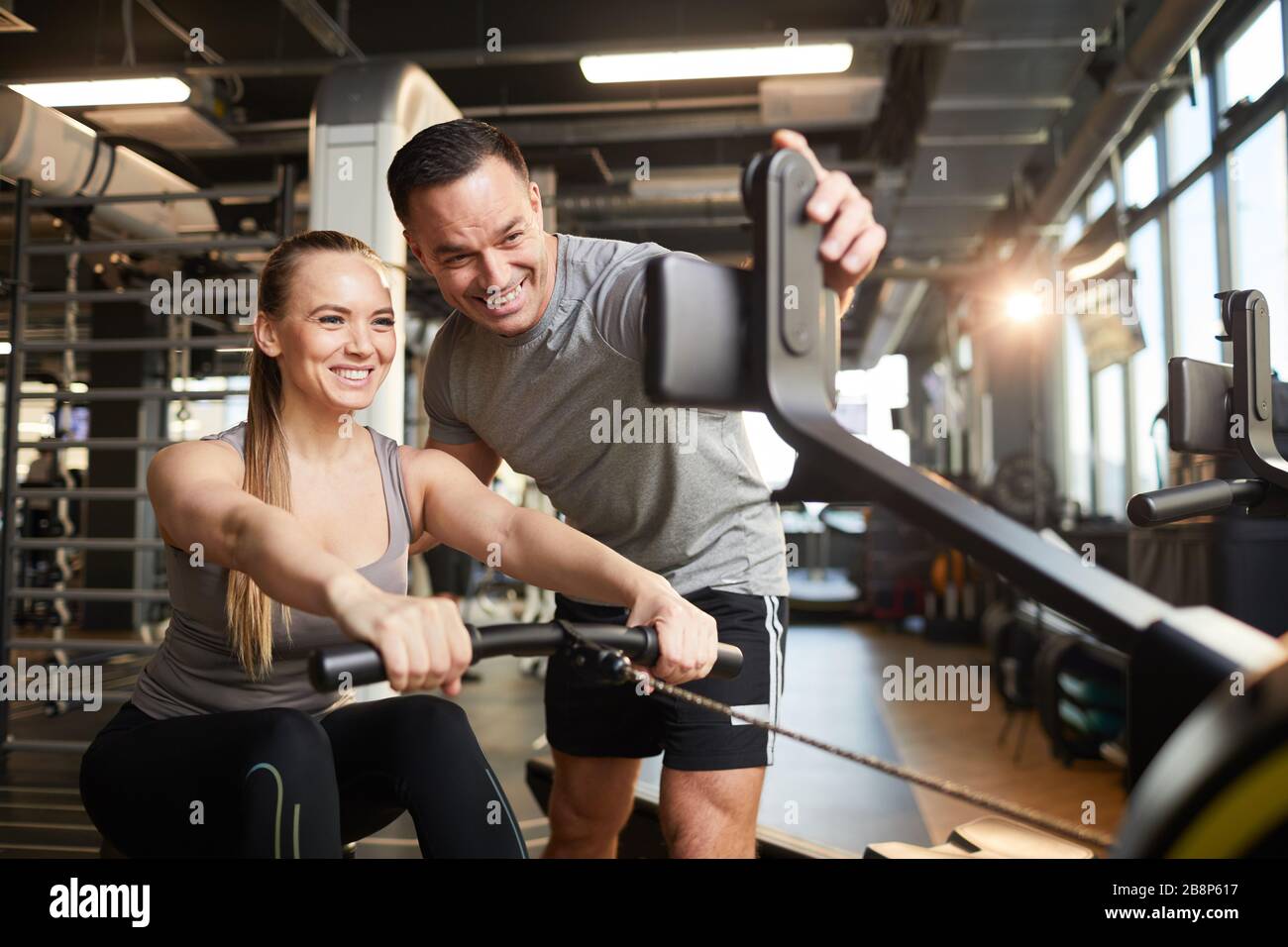 Portrait of handsome muscular coach setting up exercise machine while ...