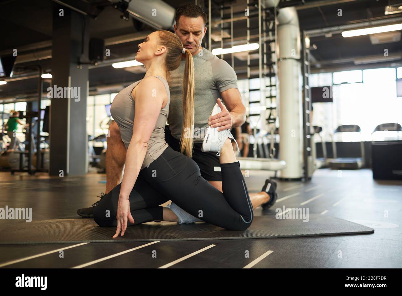 Full length portrait of muscular coach helping young woman doing ...