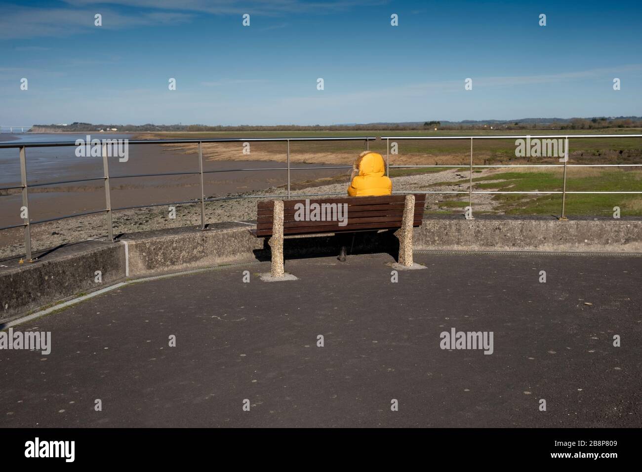 A solitary figure in a yellow jacket sitting on a bench overlooking the ...