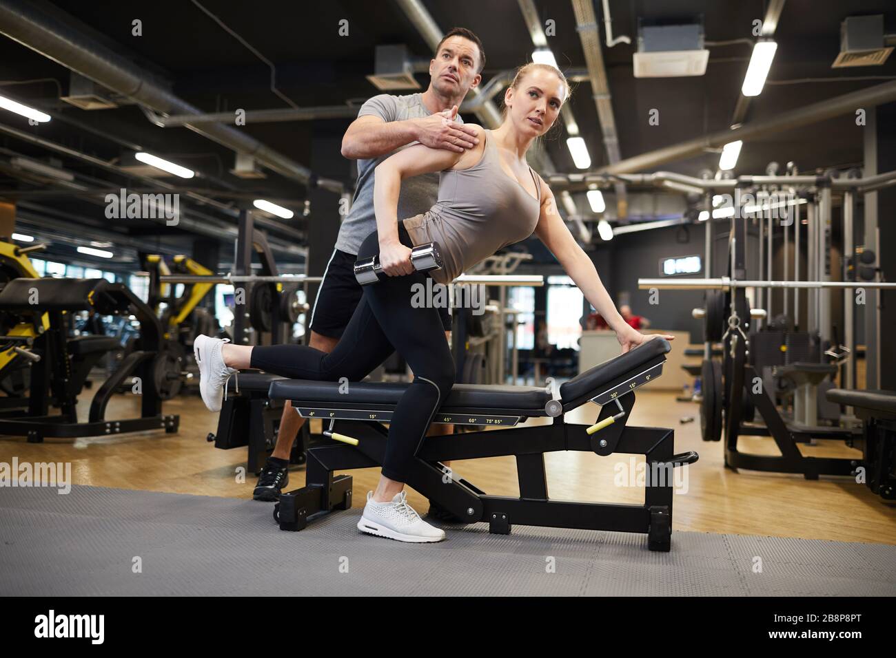 Full length portrait of muscular coach correcting position of young ...