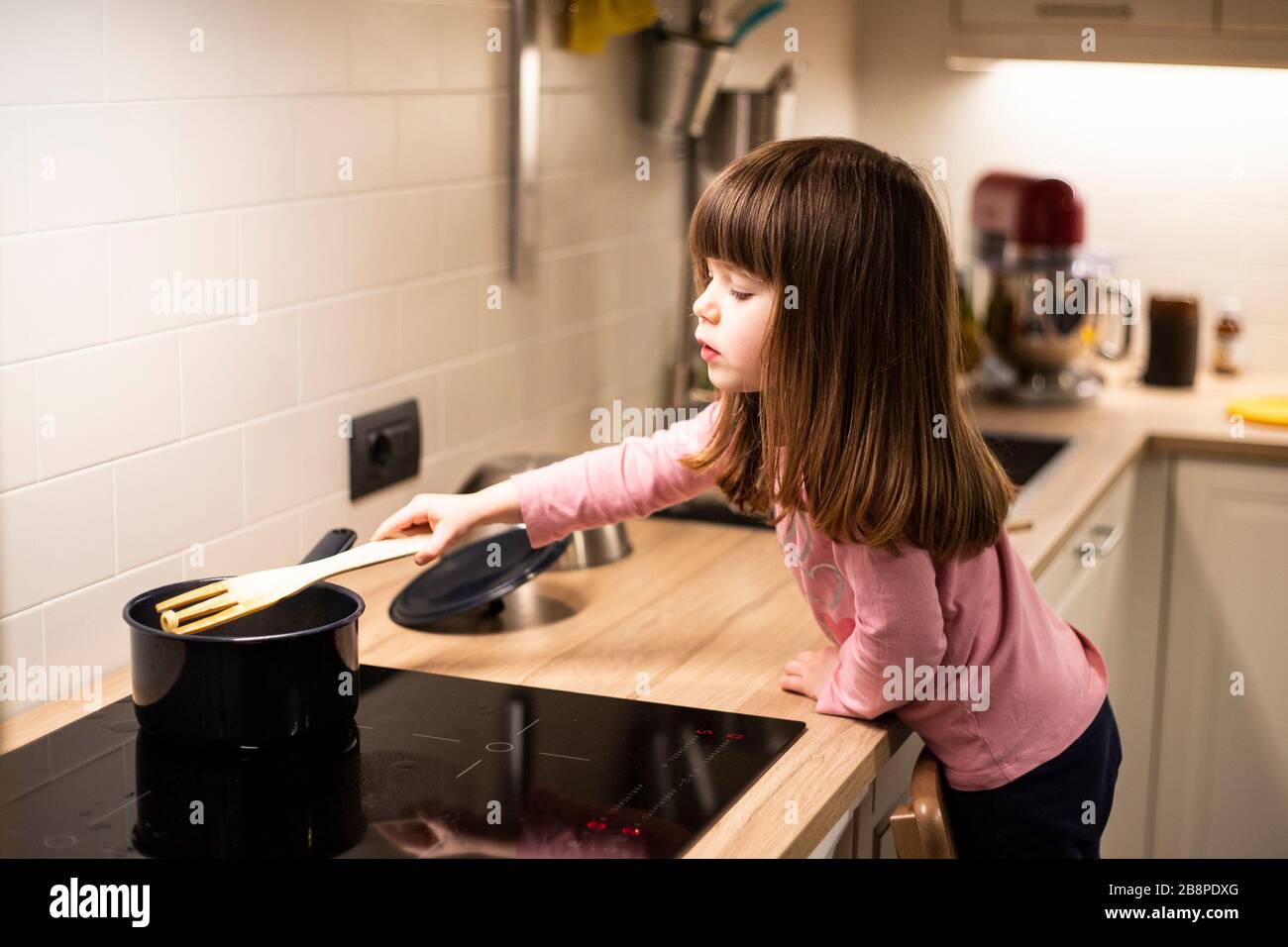 Little caucasian child, 3 years old, cooking on induction kitchen stove ...