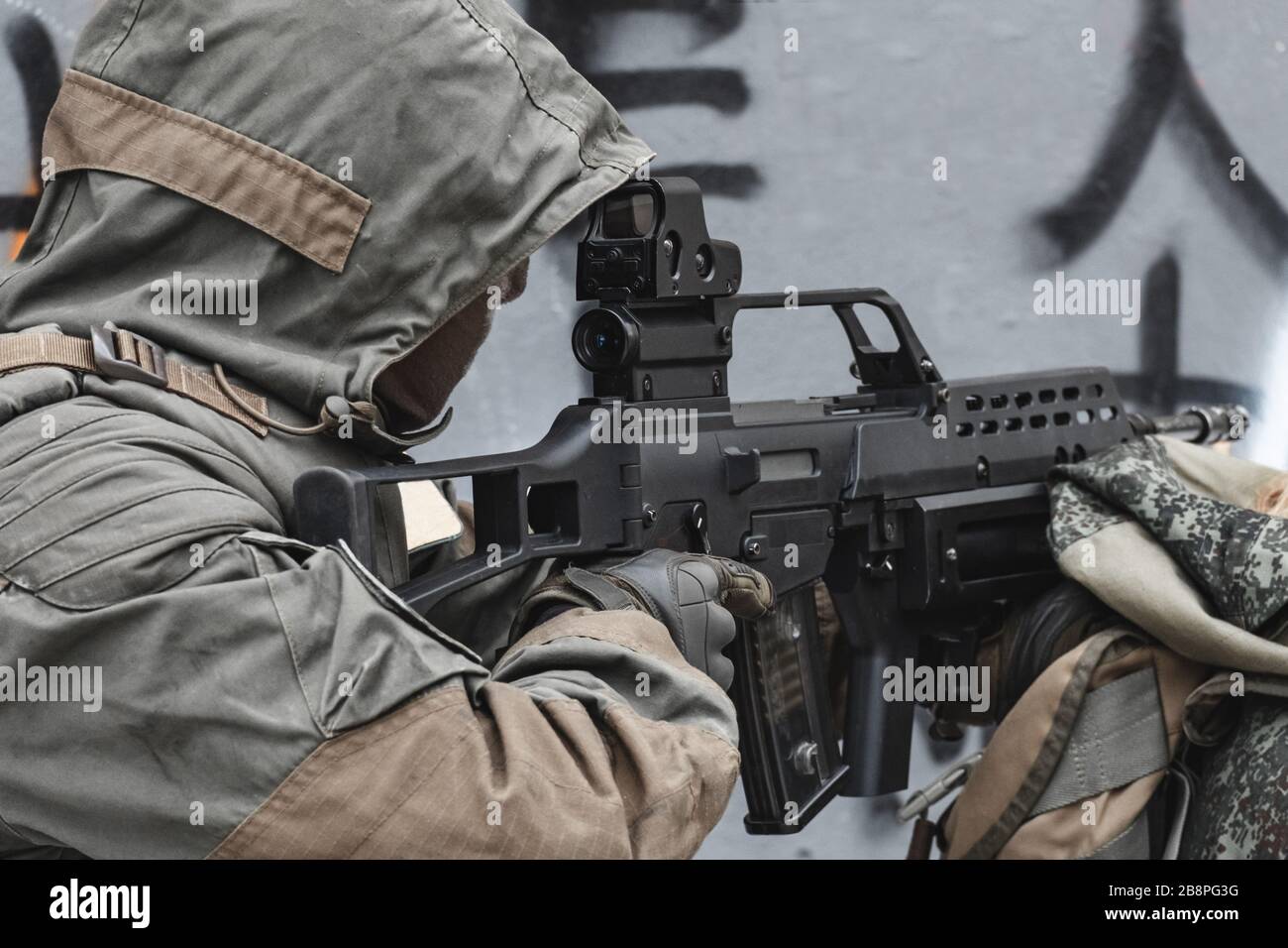 A hired soldier in the hood is aiming from a modern rifle. Close up ...
