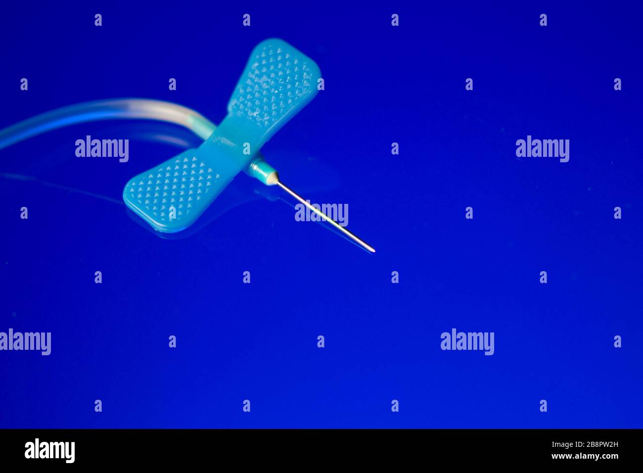 Closeup of Blue IV catheter and IV tubing on blue reflective background ...