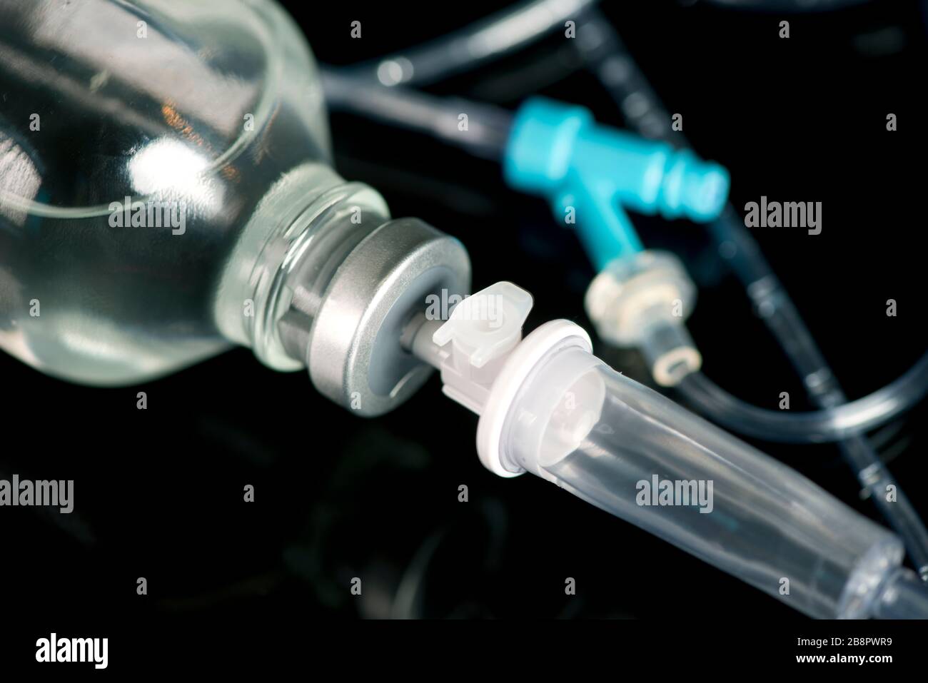 Glass IV bottle with IV drip chamber and IV tubing on dark background ...
