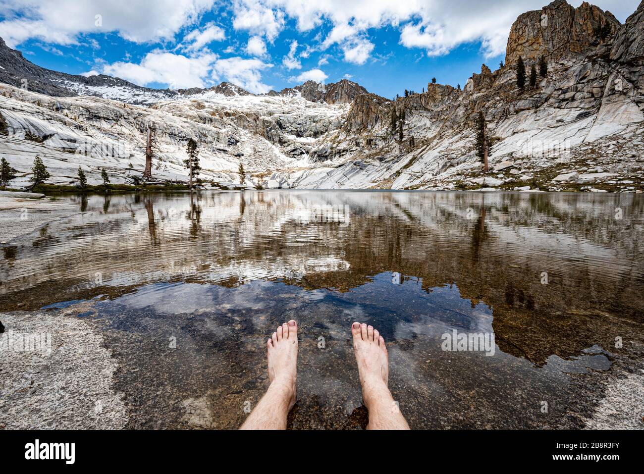 A hiker dips their feet into Pear Lake, which rests at the base of Alta ...