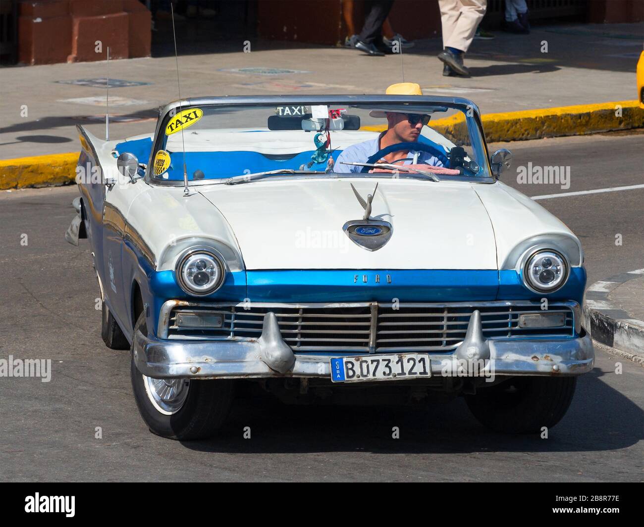 Cuban wearing hat driving a blue classic Ford car. Vintage cars are all ...