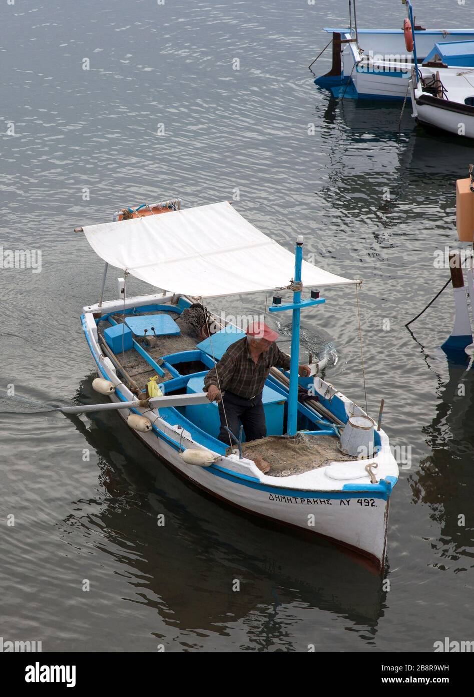 Fisherman rowing his fishing rowboat into the Greek harbor of Kamini on ...