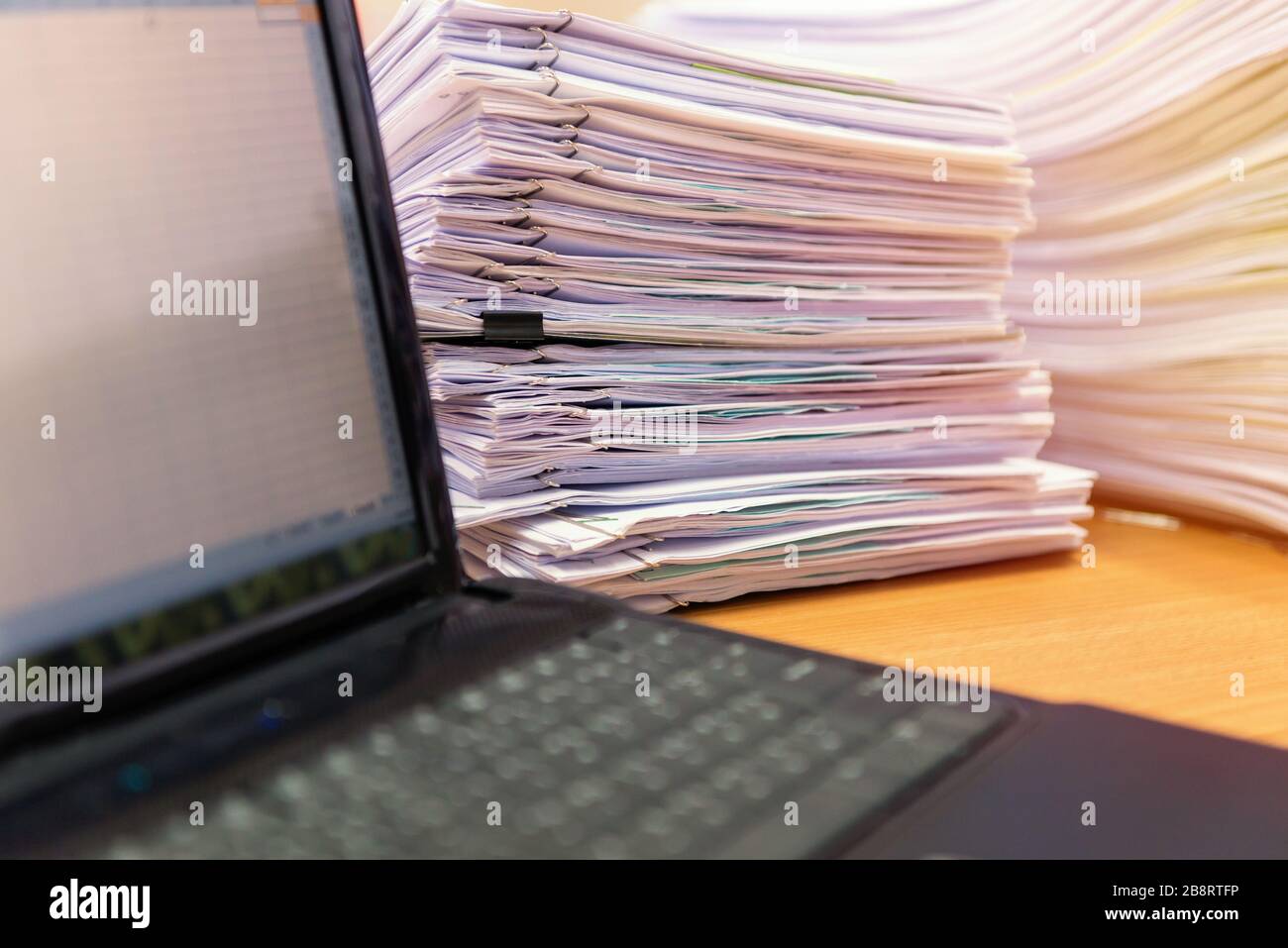 computer notebook and documents on desk stack up high waiting to be ...