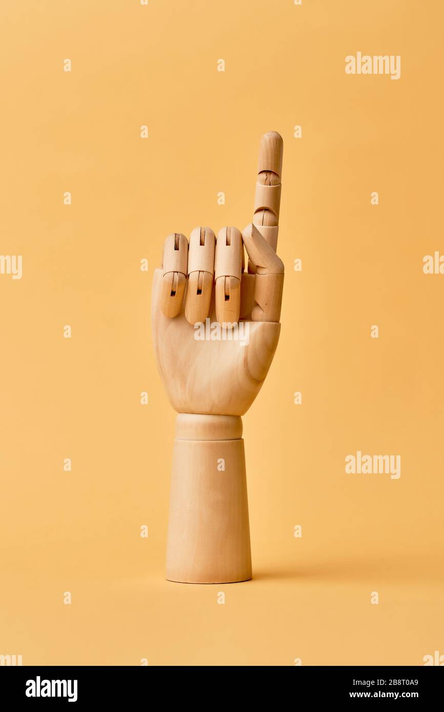 Wooden human hand with finger raised up on blank orange background ...