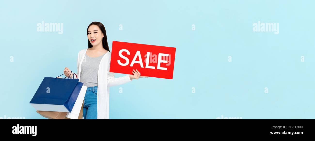 Surprised Asian woman holding red sale sign isolated on light blue ...