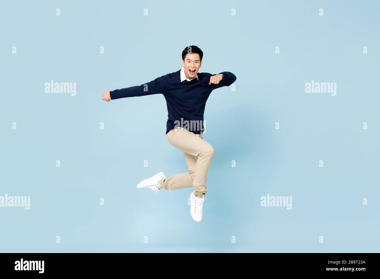 Young handsome Asian man smiling and jumping in mid-air on light blue ...