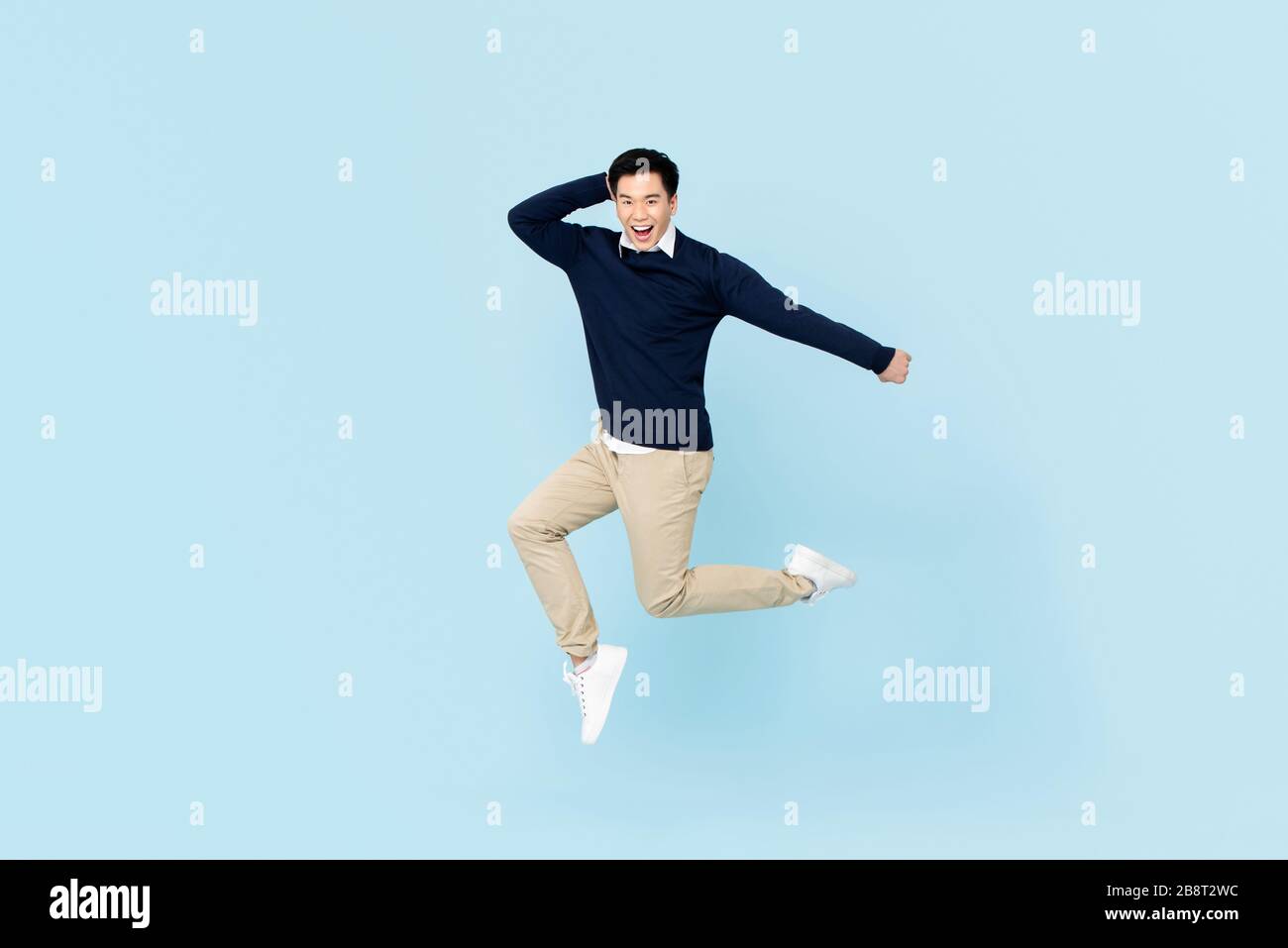 Smiling young handsome Asian man jumping on light blue studio ...