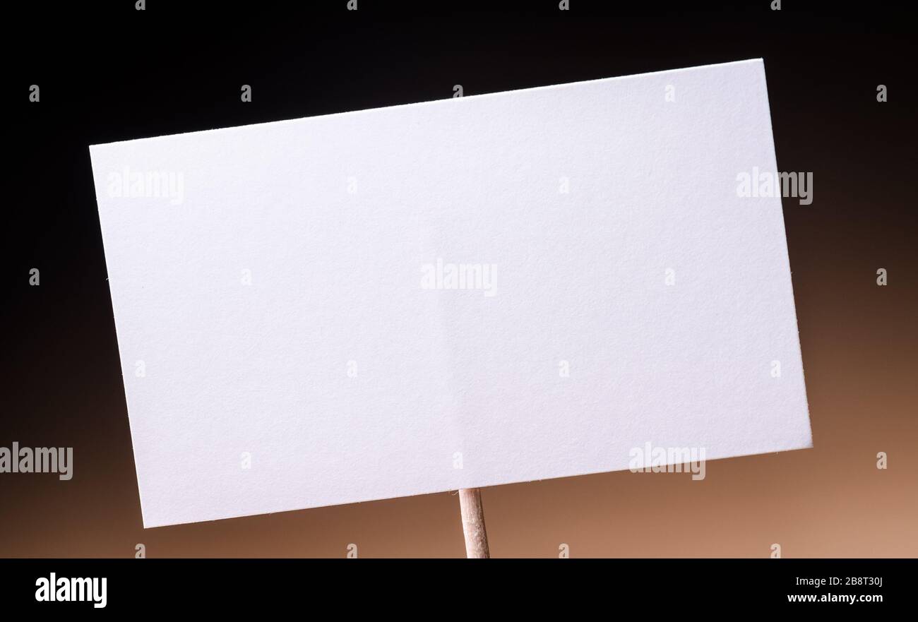 Blank, empty, white cardboard sign on wooden stick against dark ...