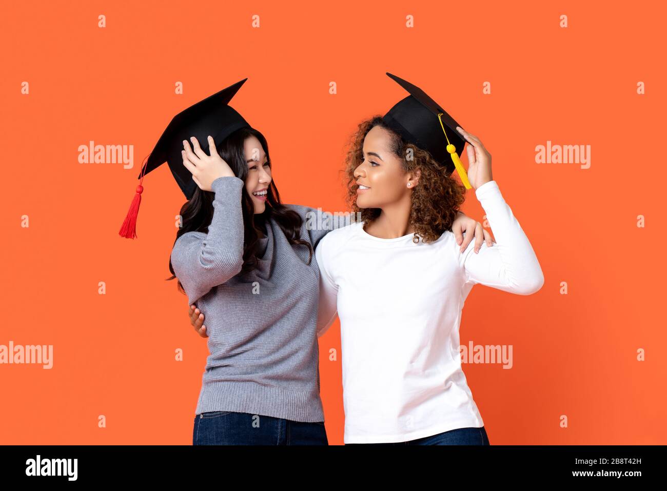 Portrait of two happy mixed-race women graduating holding there ...