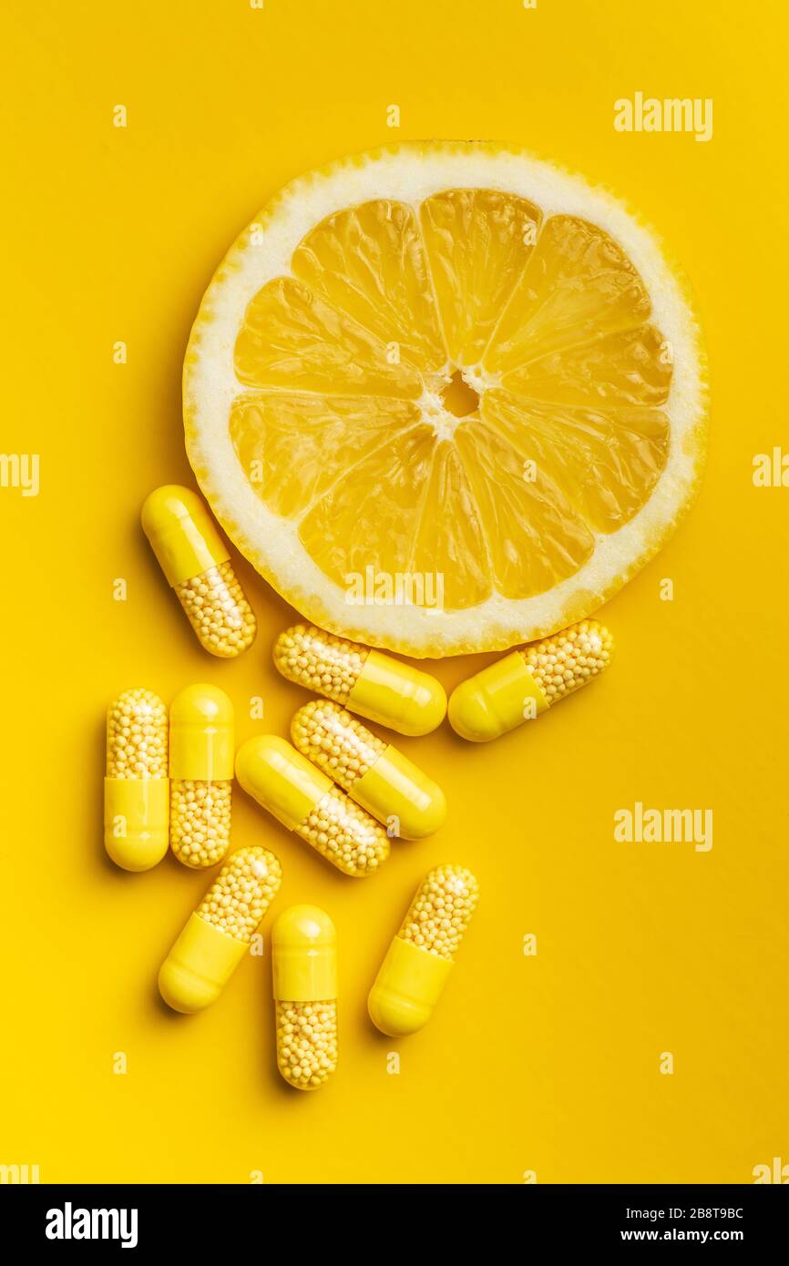 Vitamin capsules. Vitamin C pills and slice of lemon on yellow ...